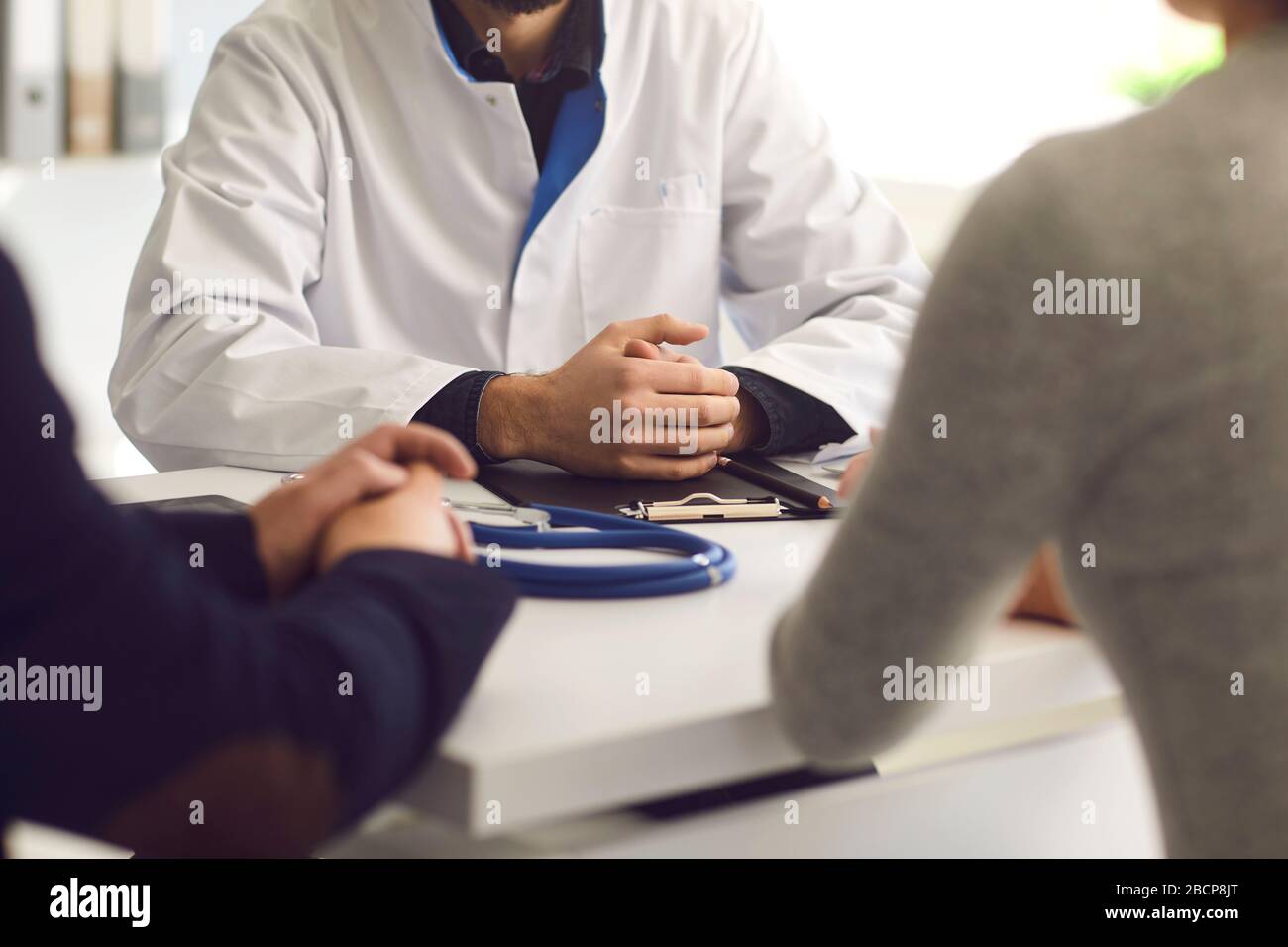 Confident doctor and couple patient sitting at the table in clinic ...