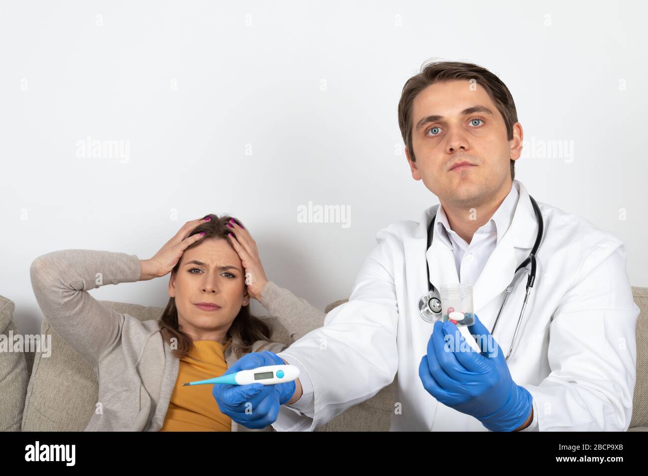 Young male doctor consulting female patient with influenza symptoms at ...