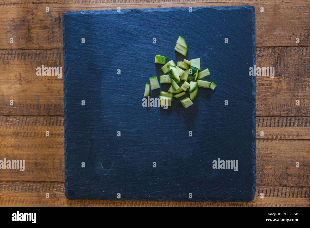 Top view of courgettes cut into pieces on a slate plate and wooden ...