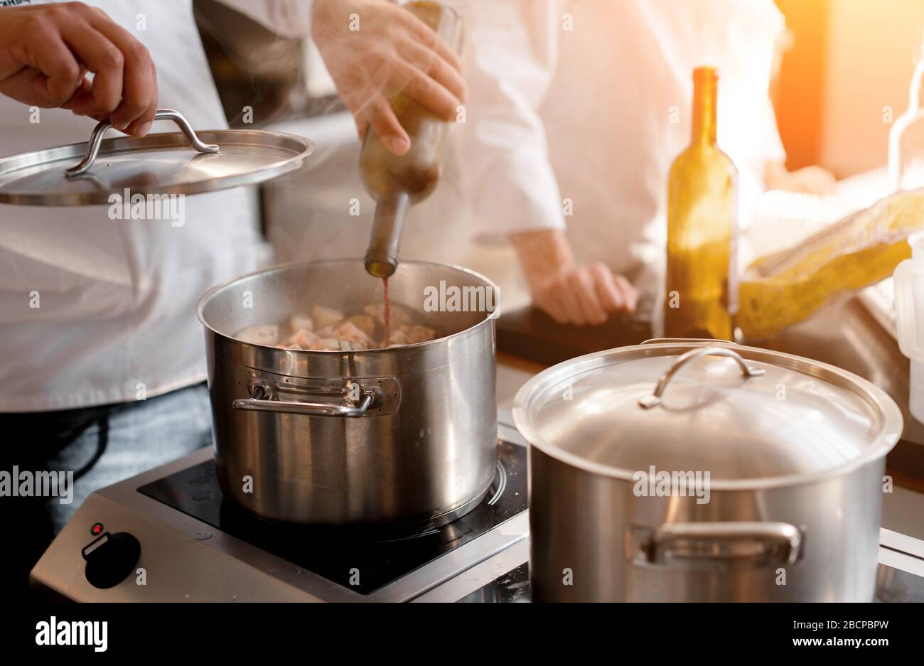 Closeup hands of unrecognizable chef pouring wine into pot with meat ...