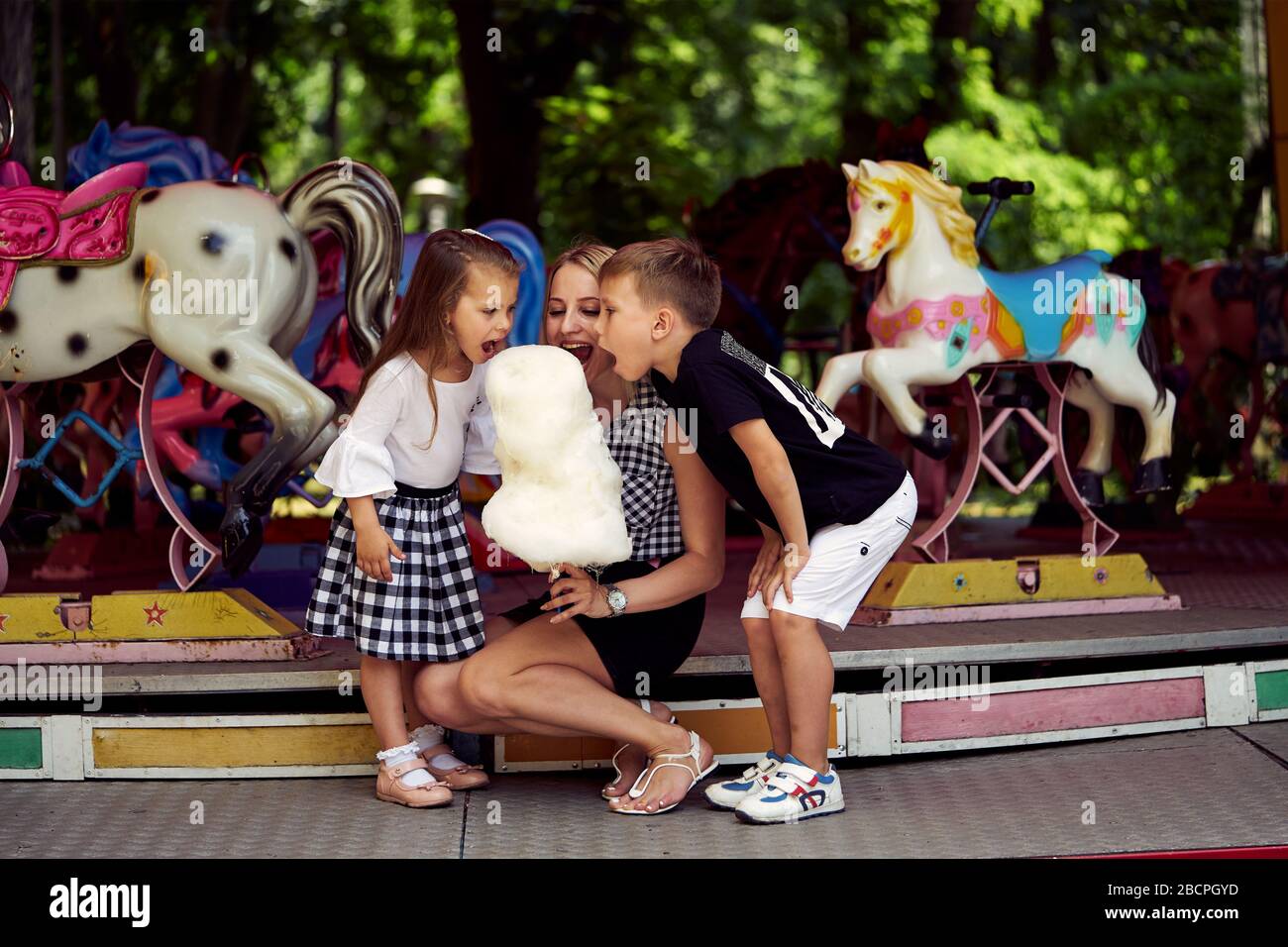 Happy family eating cotton candy at an amusement park. Mother, son and ...