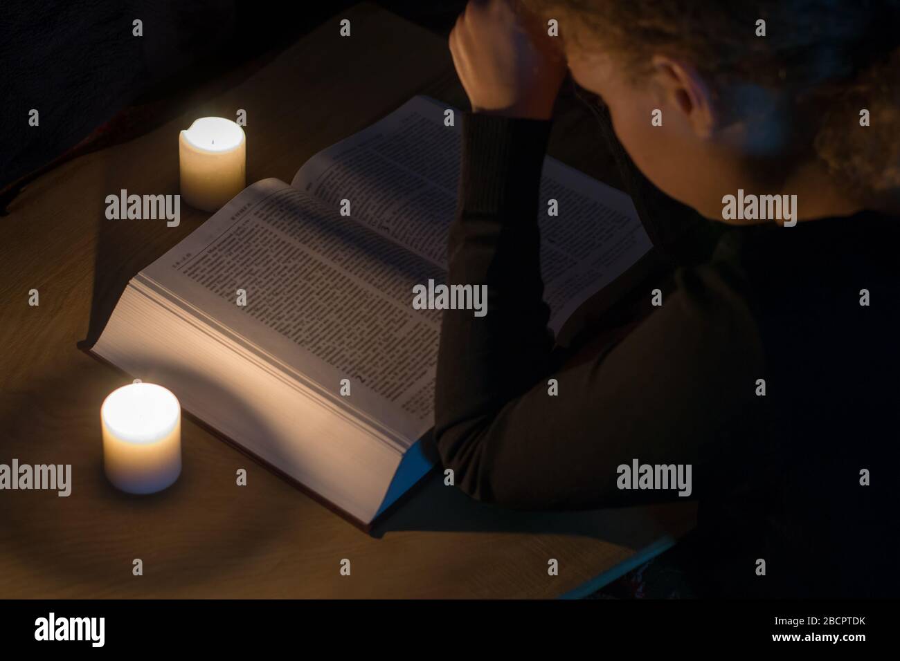Praying girl over the bible by candlelight Stock Photo - Alamy