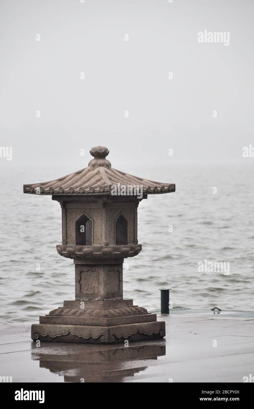 A traditional Chinese stone lantern stands on the edge of West Lake in ...
