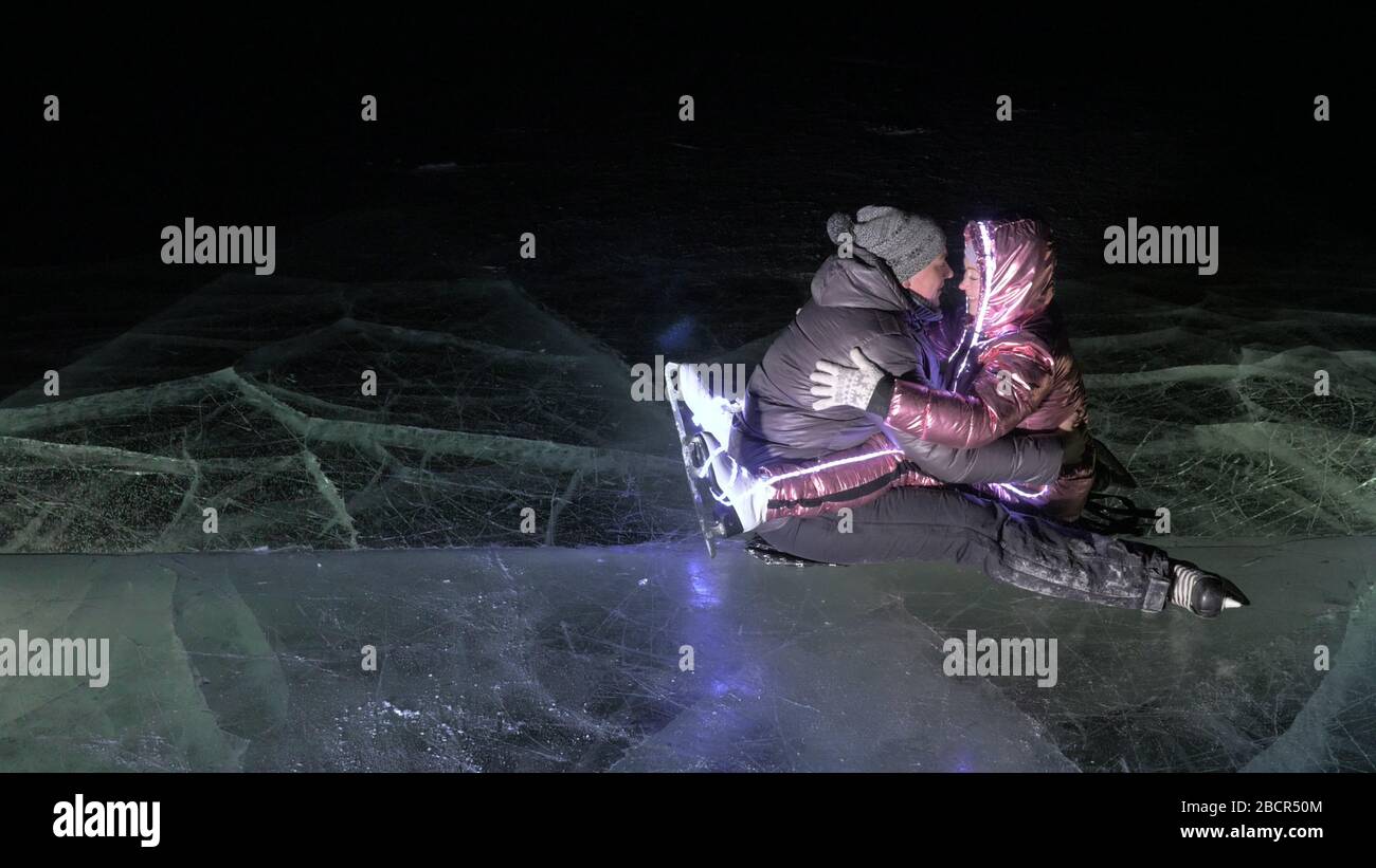Young loving couple skating at ice rink at night. Man and woman kiss ...