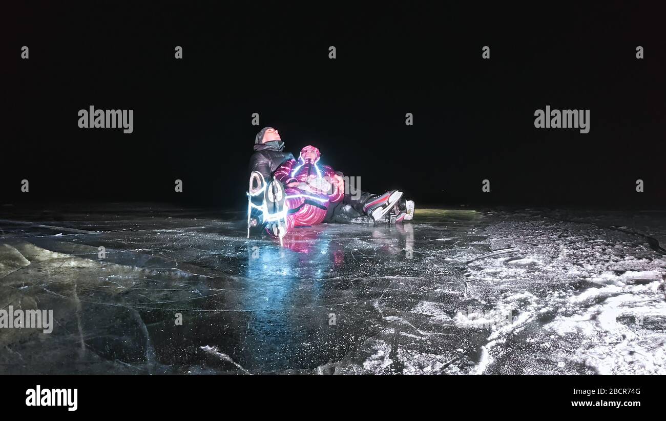 Young loving couple skating at ice rink at night. Man and woman kiss ...