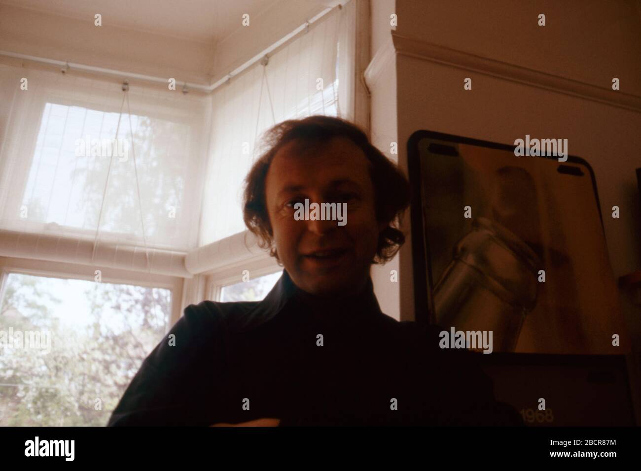 A dad standing in the back room of the family home, smiling at the ...