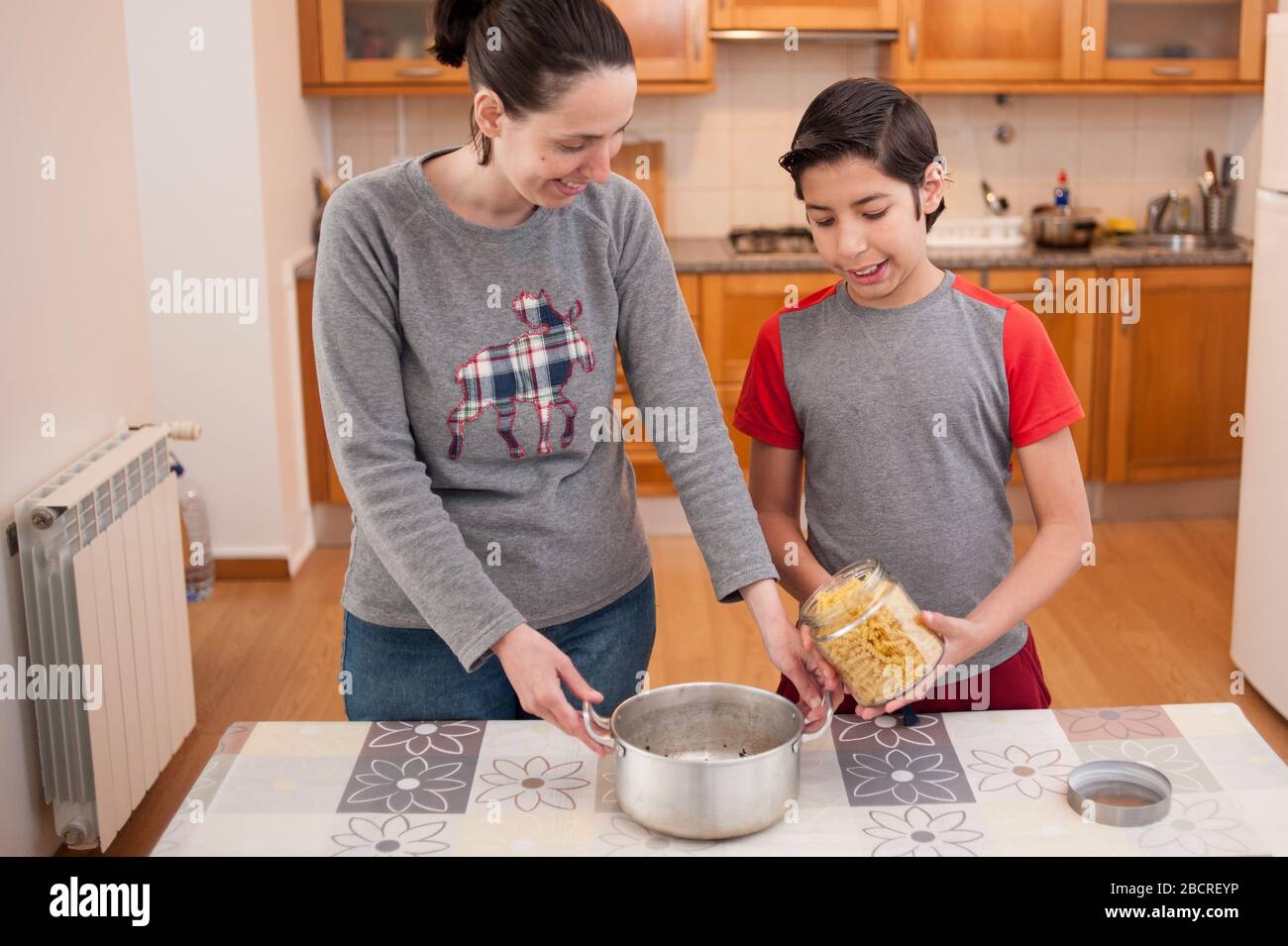 mom and son cooking pasta together. He is opening the bottle and the ...