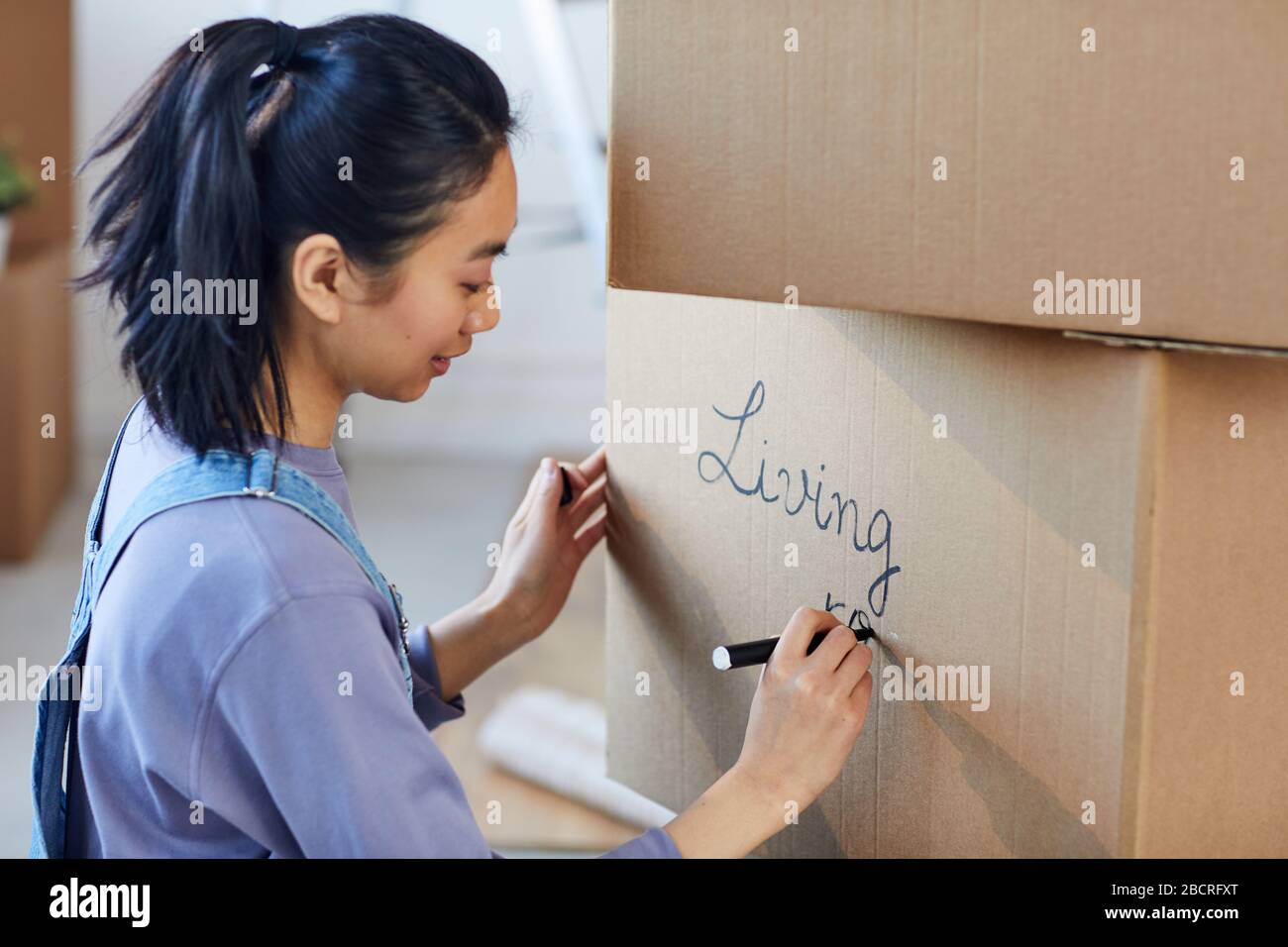 Side view portrait of smiling Asian woman writing on cardboard box ...