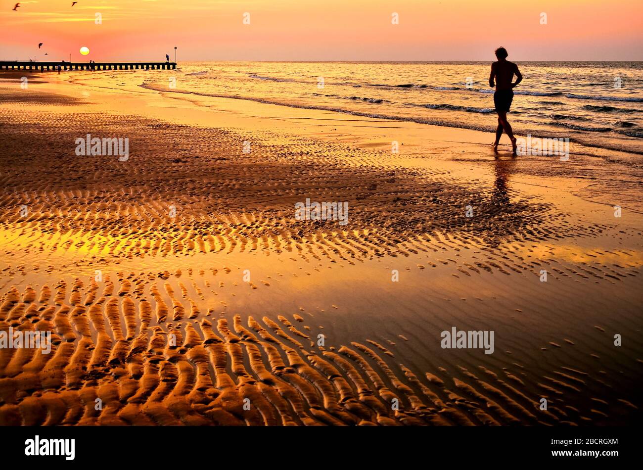 Silhouette of young man running on beach sand at sunrise. Original ...