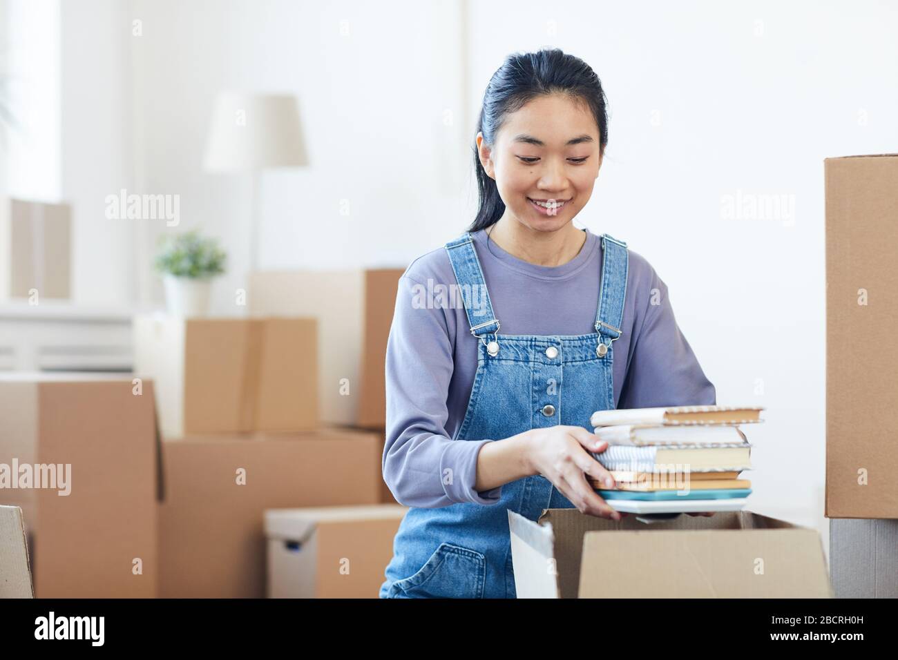 Portrait of young Asian woman packing books to cardboard boxes and ...