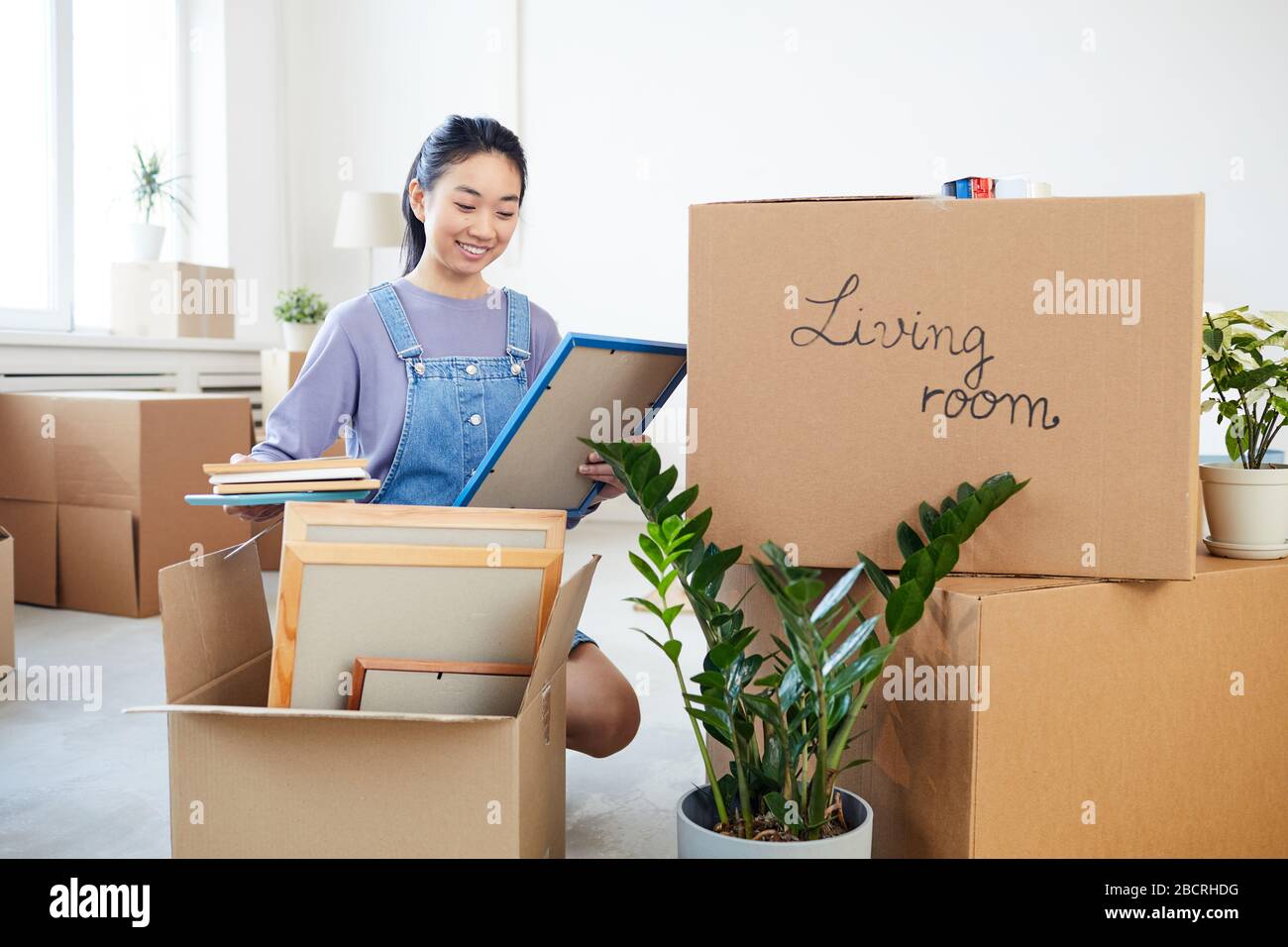 Full length portrait of young Asian woman packing decor items to ...