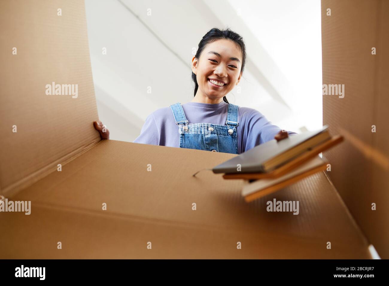 Low angle view at young Asian woman looking into cardboard box and ...