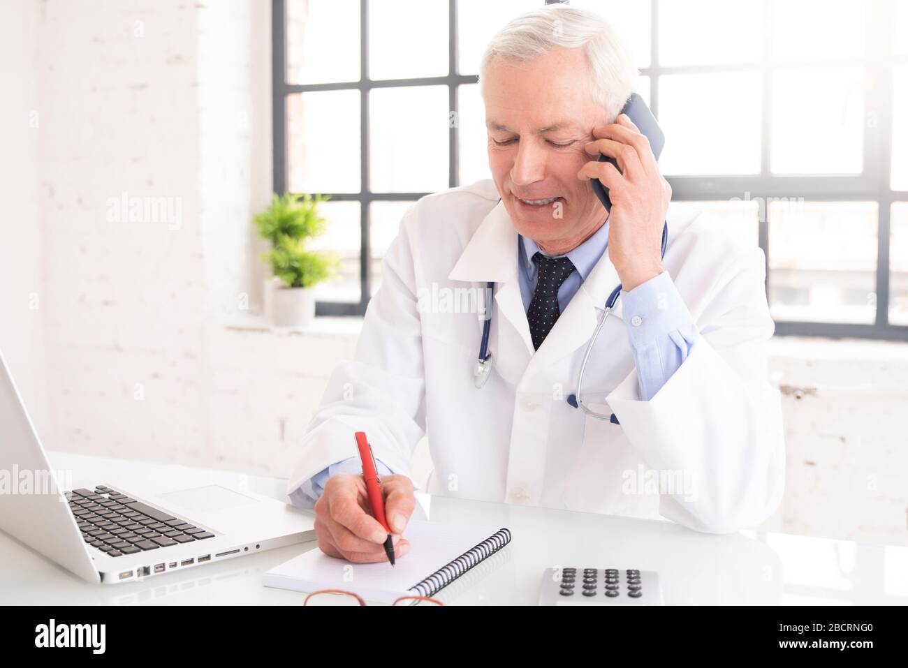 Shot of senior male doctor using mobile phone and talking with his ...