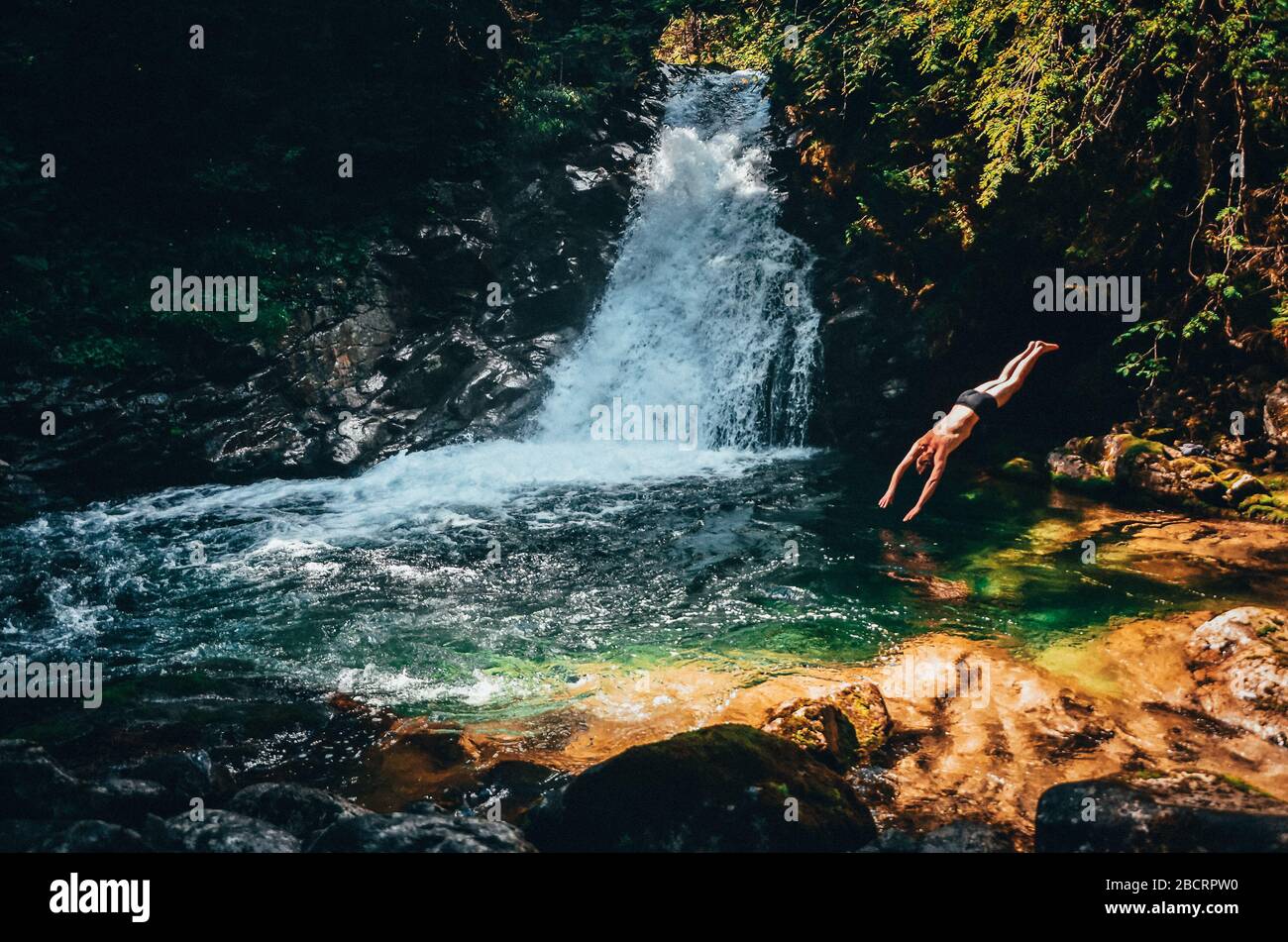Man jump cliff jump into clean water in wild waterfall hidden in green ...