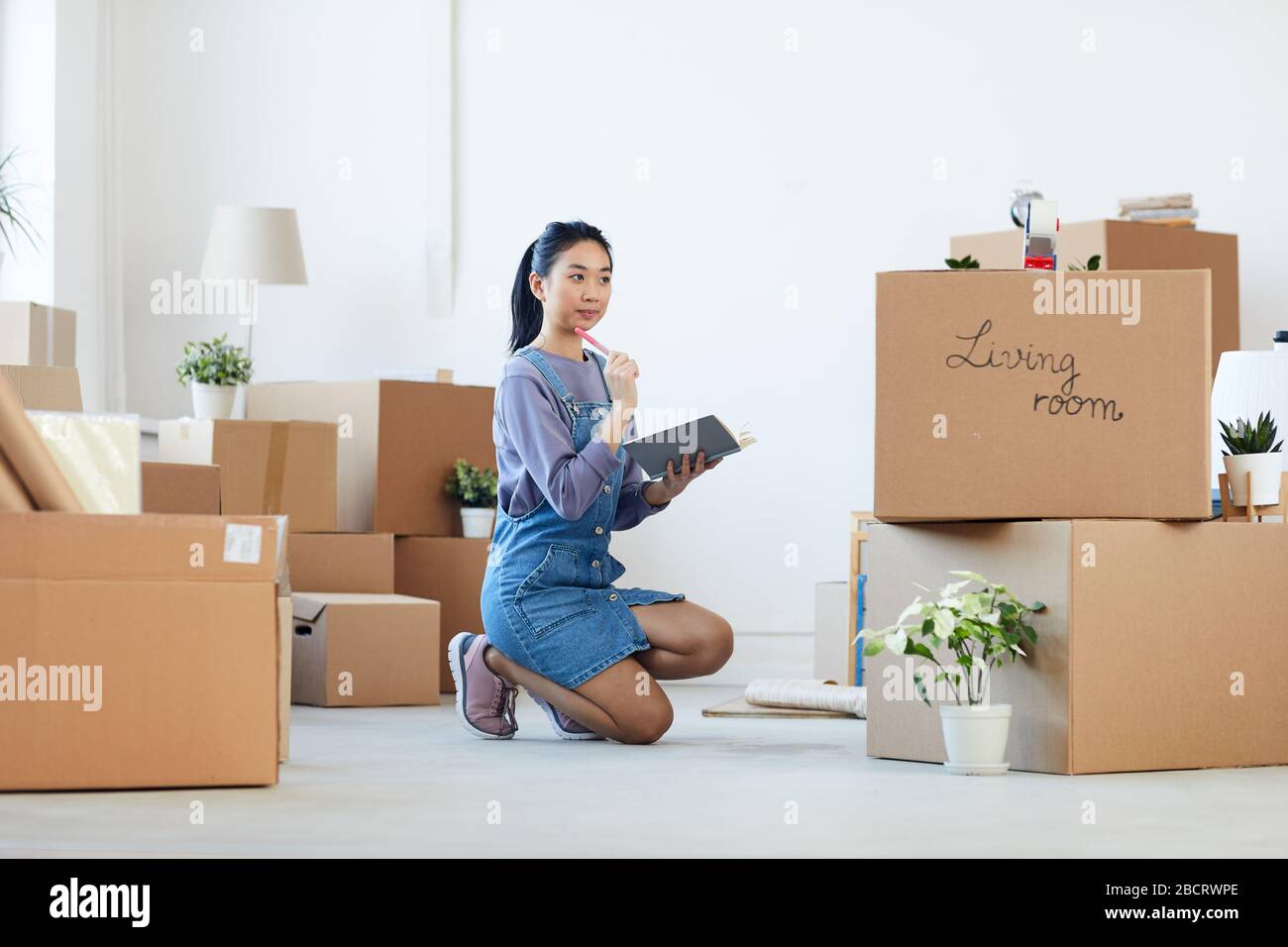 Full length portrait of young Asian woman organizing moving in process ...