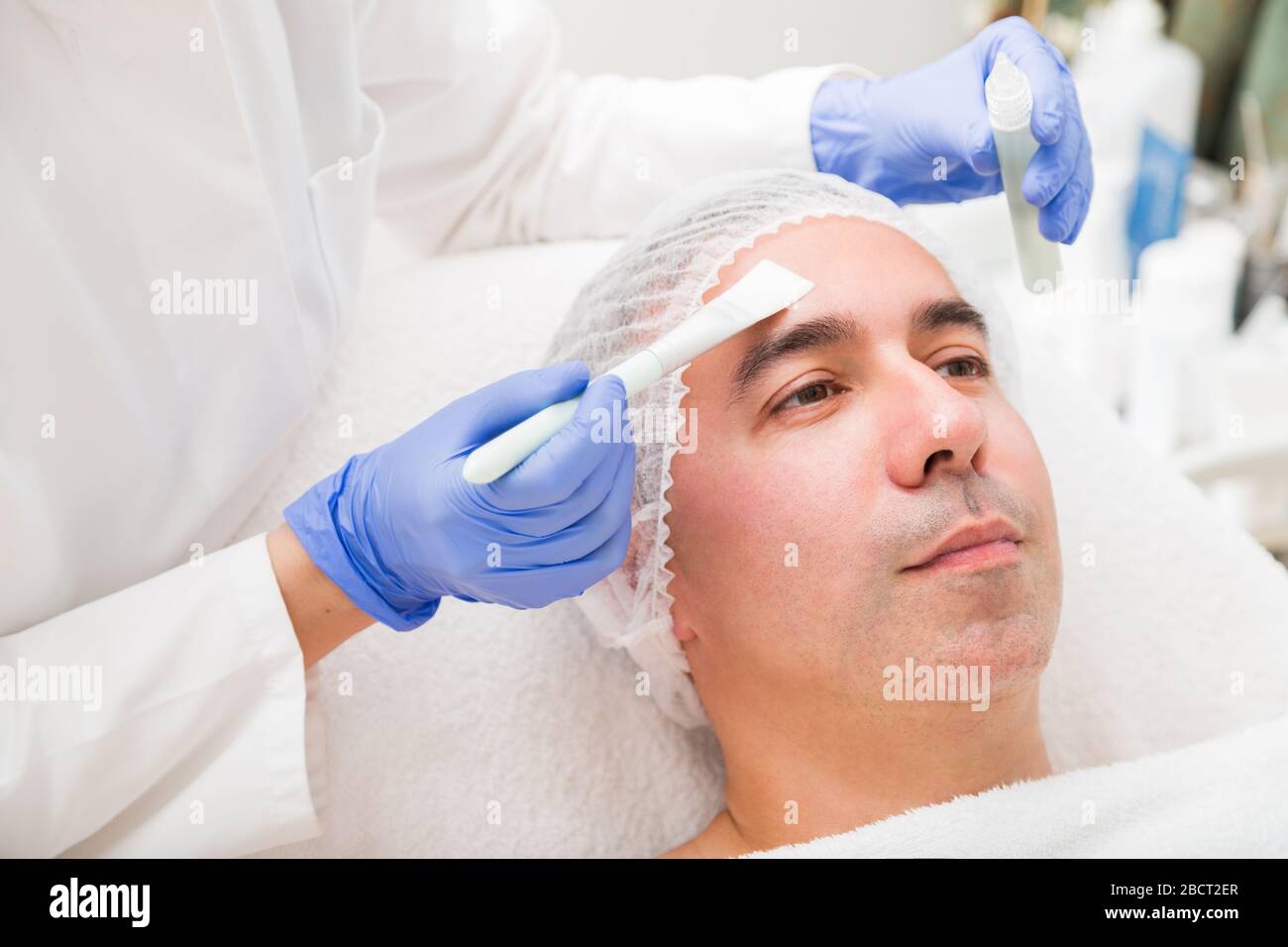 Woman's hands make man facial mask in beauty salon Stock Photo - Alamy