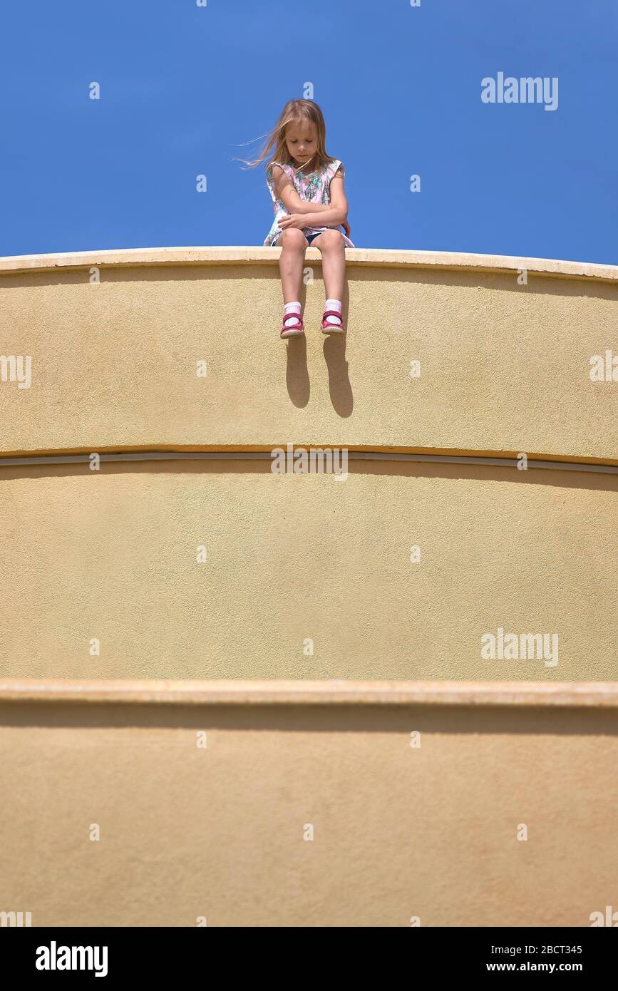little girl sits on the edge of the wall dangling legs, stone wall her ...