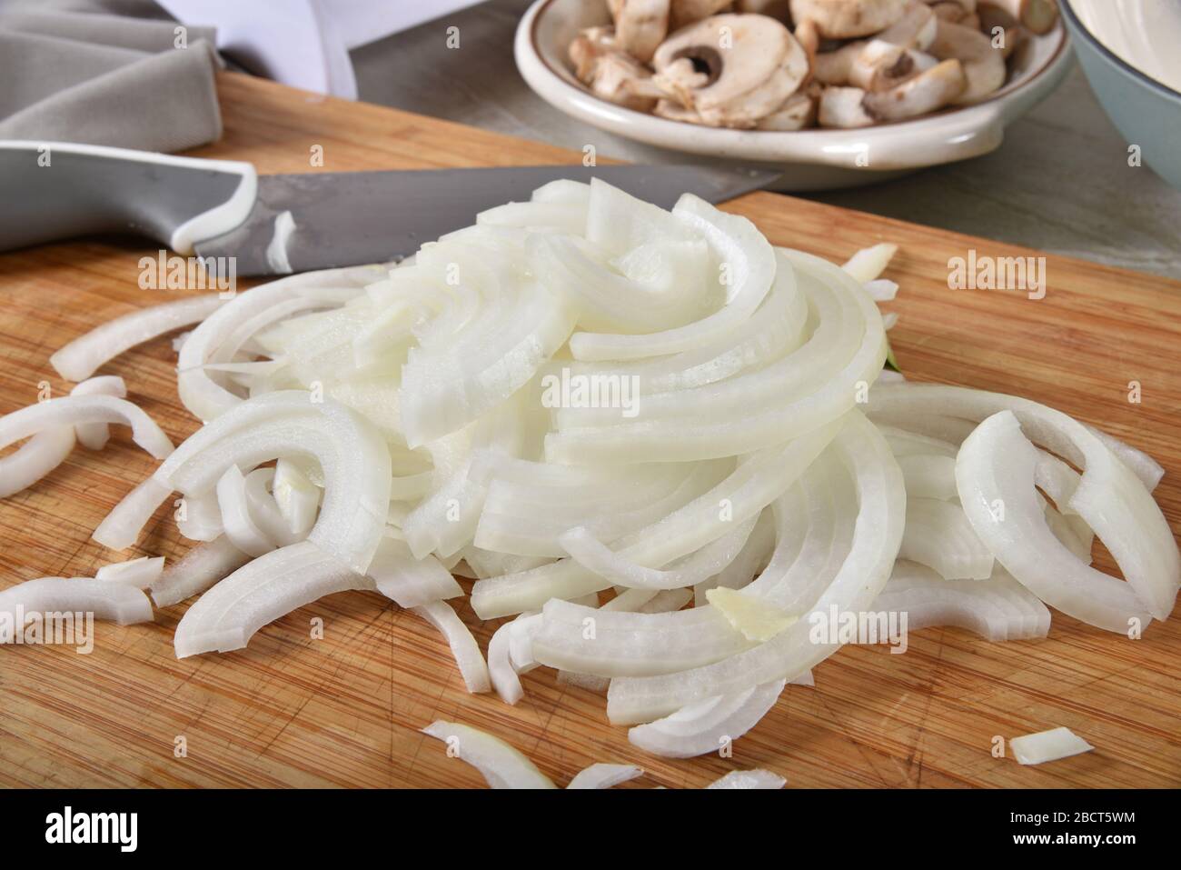 Thin sliced onions on a cutting board with sliced mushrooms Stock Photo ...
