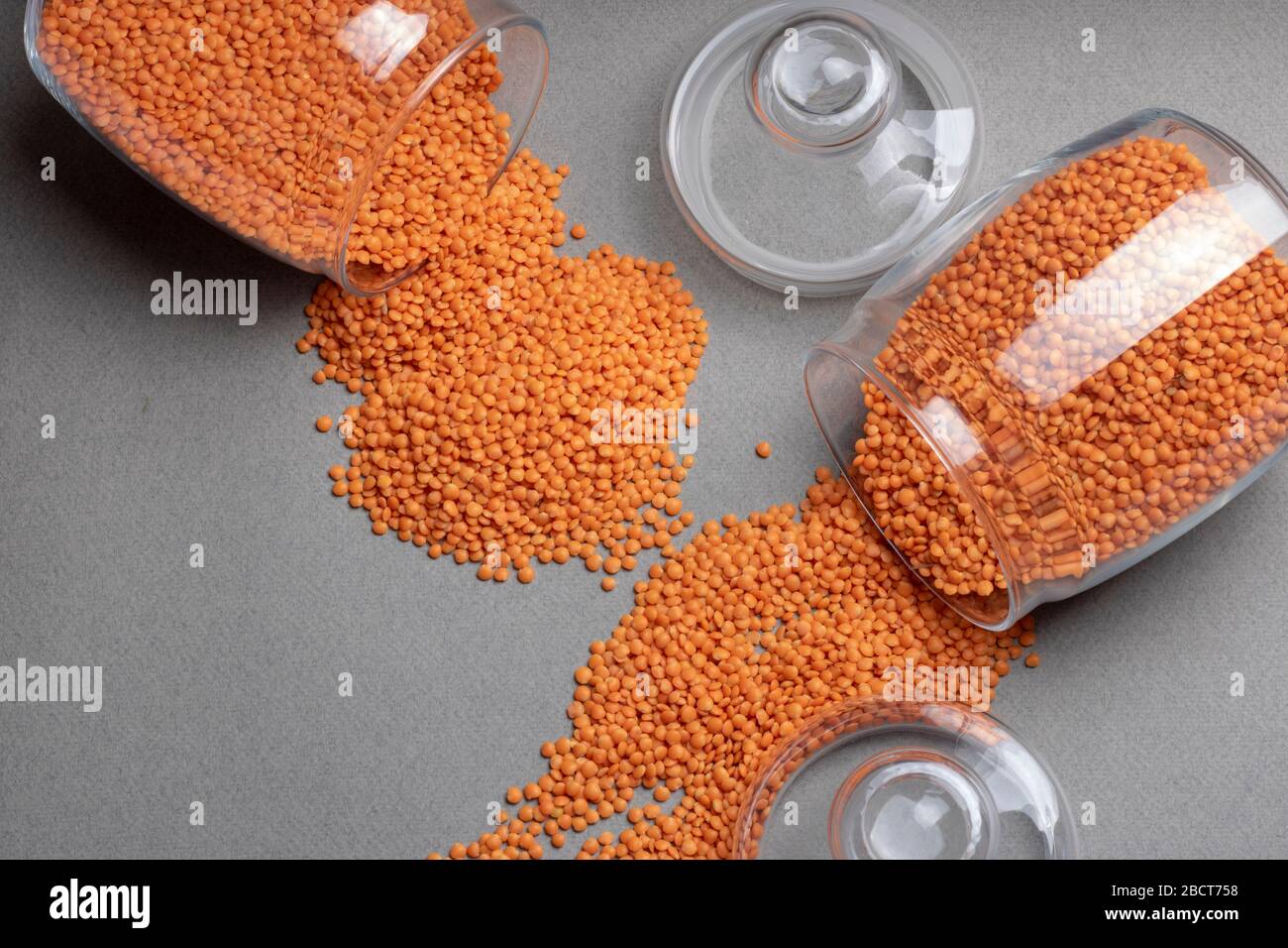 Red lentils spilled from glass jars onto gray paper, top view Stock ...
