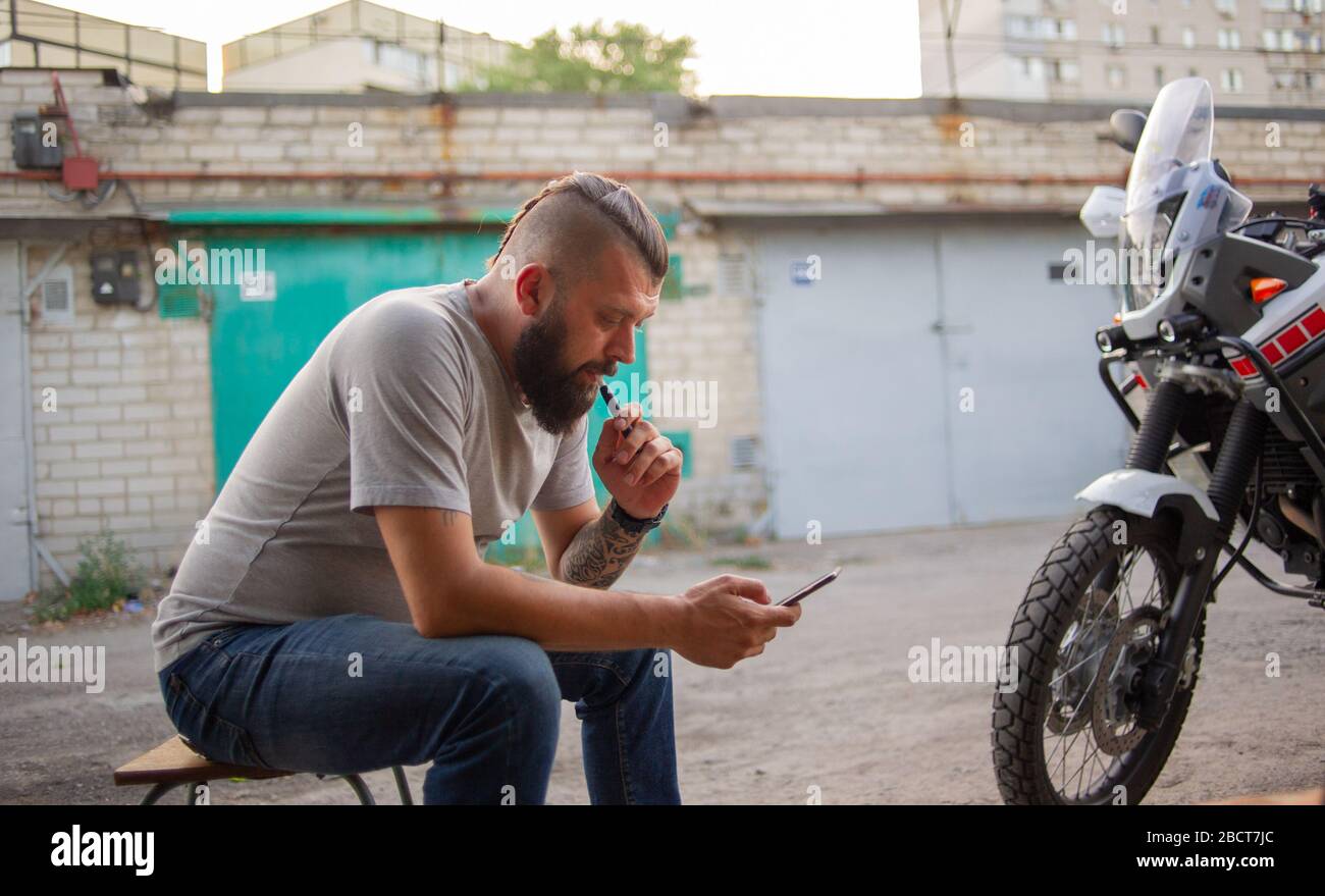 Thoughtful man having rest near bike. Male biker smokes near a bike. A ...