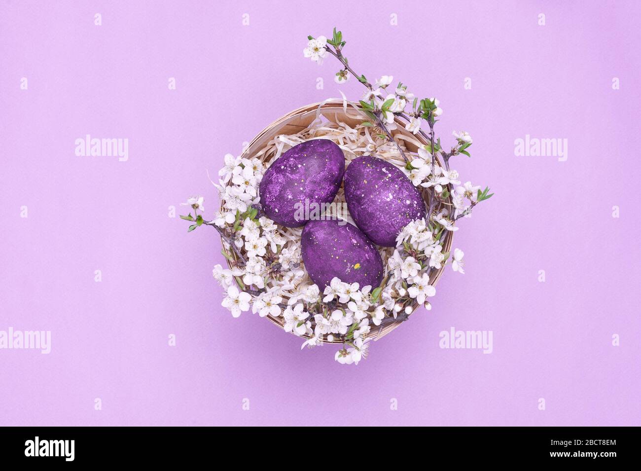 Violet easter eggs in a basket with flowers on a violet background ...