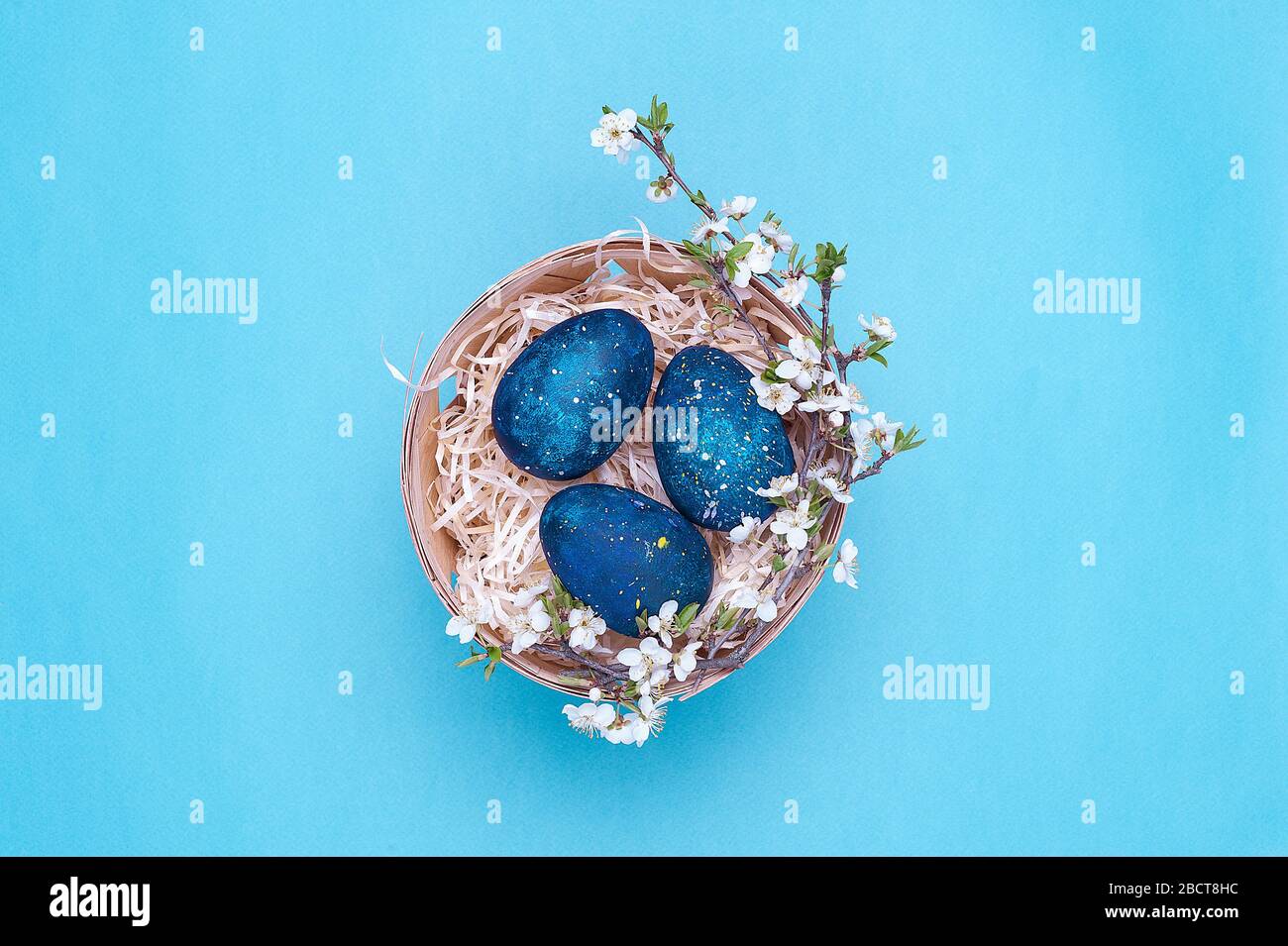 Azure easter eggs in a basket with flowers on a violet background ...