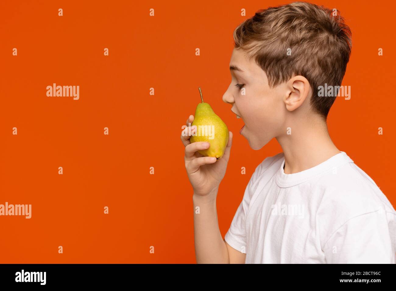 Teen boy biting fresh pear, side view Stock Photo - Alamy