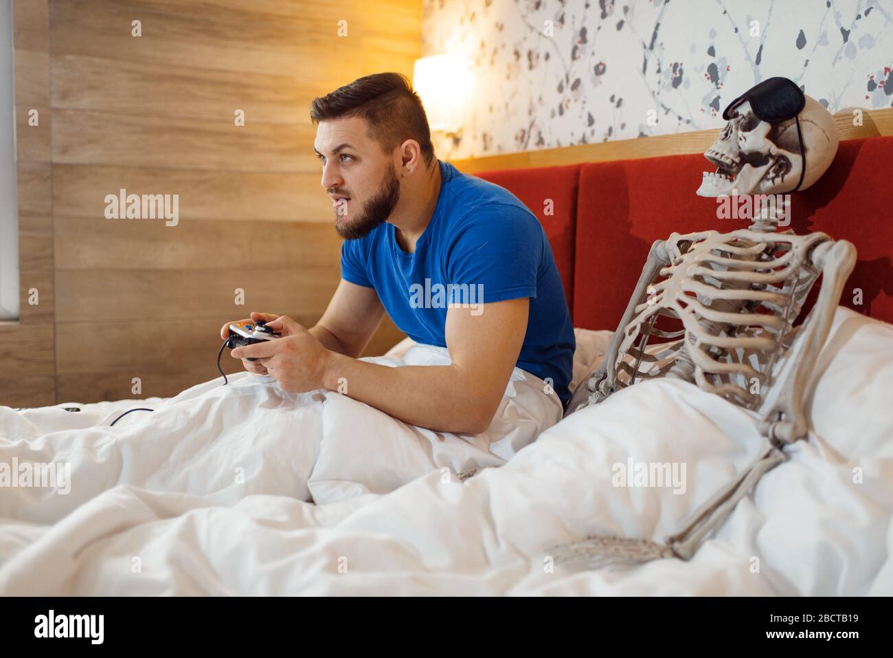 Man playing game console, wife skeleton in the bed Stock Photo - Alamy