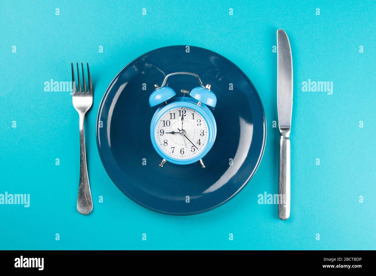 Alarm clock with fork and knife on the blue plate on blue table. Time ...
