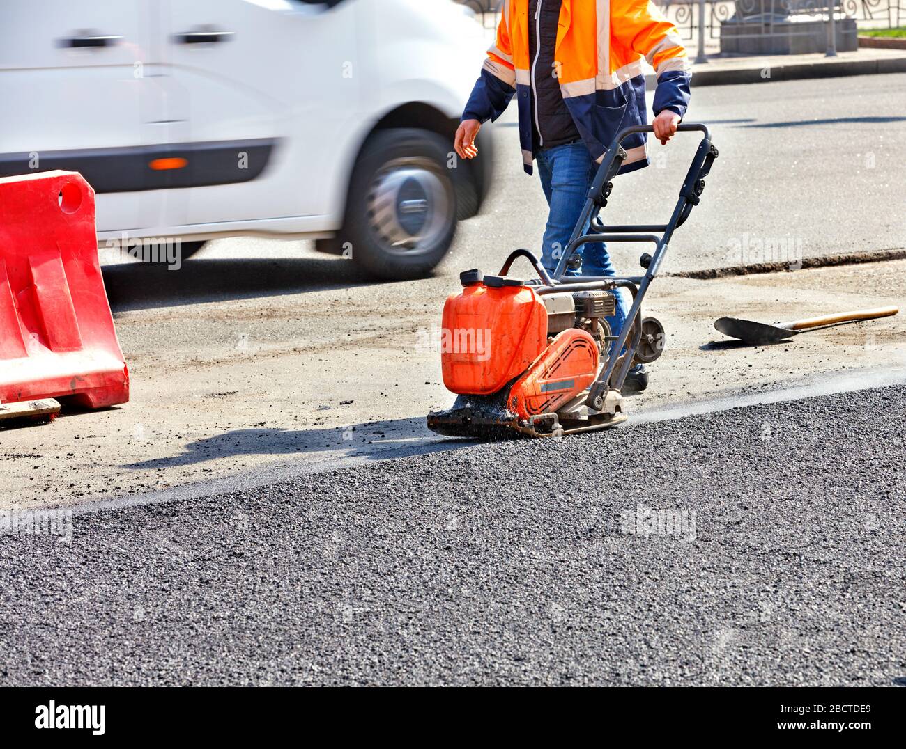 A road worker compacts asphalt on the carriageway with a gasoline ...