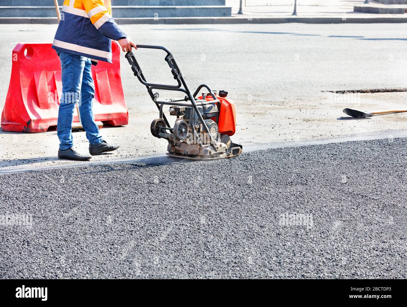 A road worker compacts asphalt in a fenced section of the road on the ...