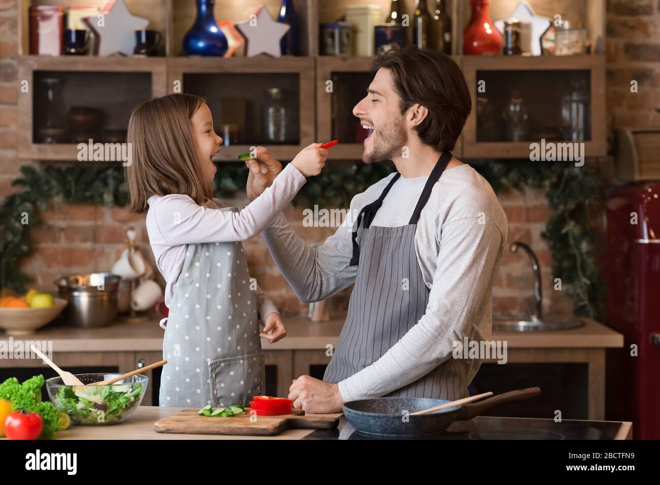 Girl and her father feeding each other with vegetables while cooking ...