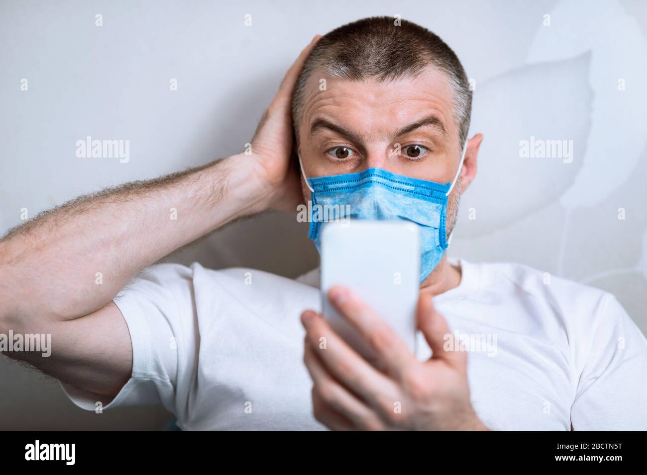 Scared Man In Mask Using Phone Sitting At Home Stock Photo - Alamy