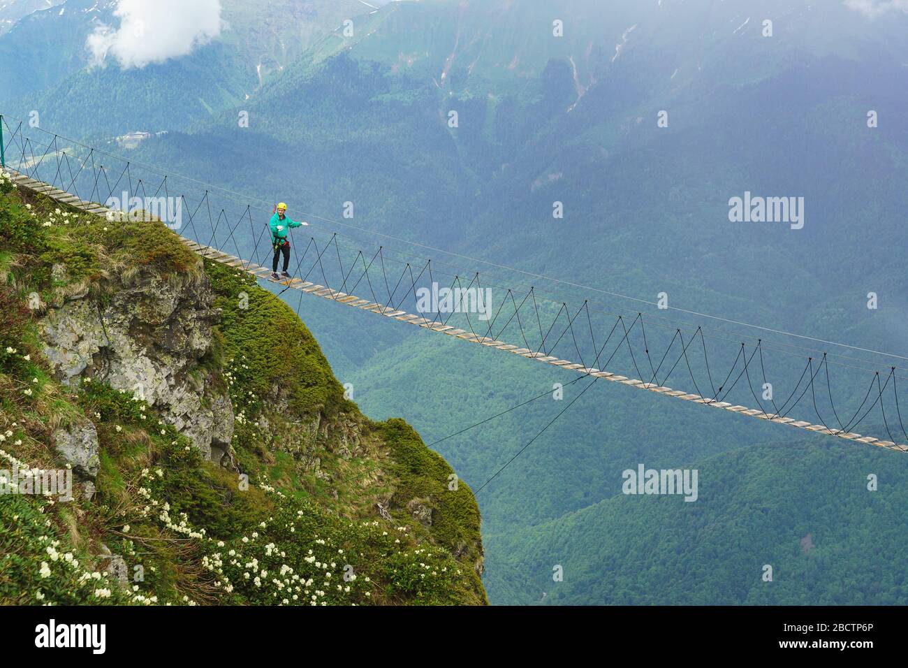 A tourist in a helmet and safety ropes is stretched between the cliffs ...