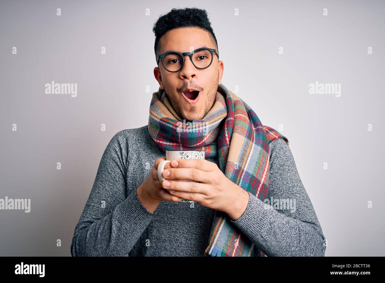 Young handsome man wearing scarf drinking mug of hot coffe over ...
