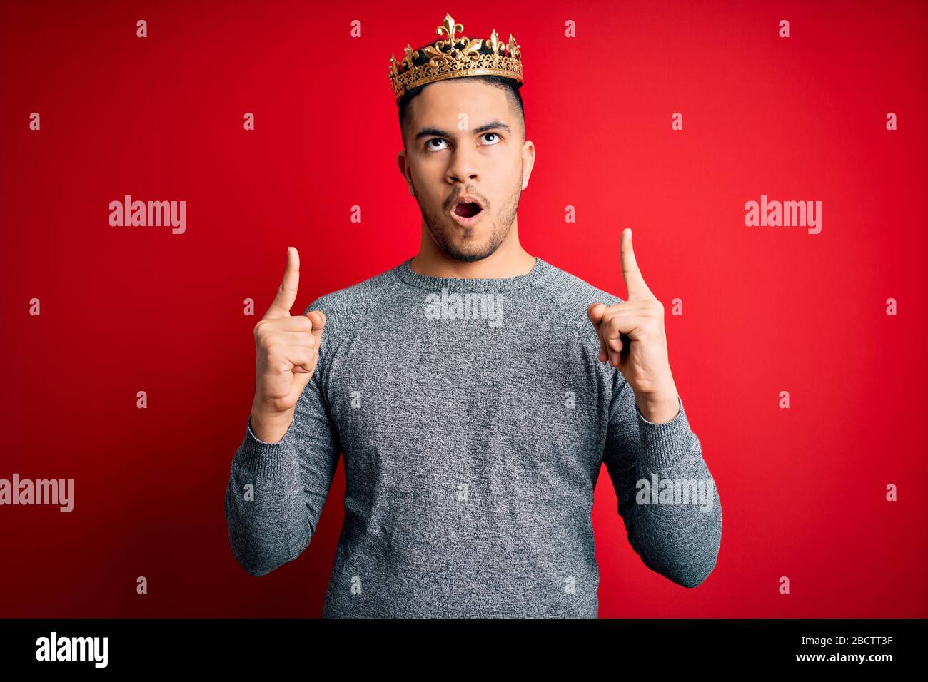 Young handsome man wearing golden crown of prince over isolated red ...