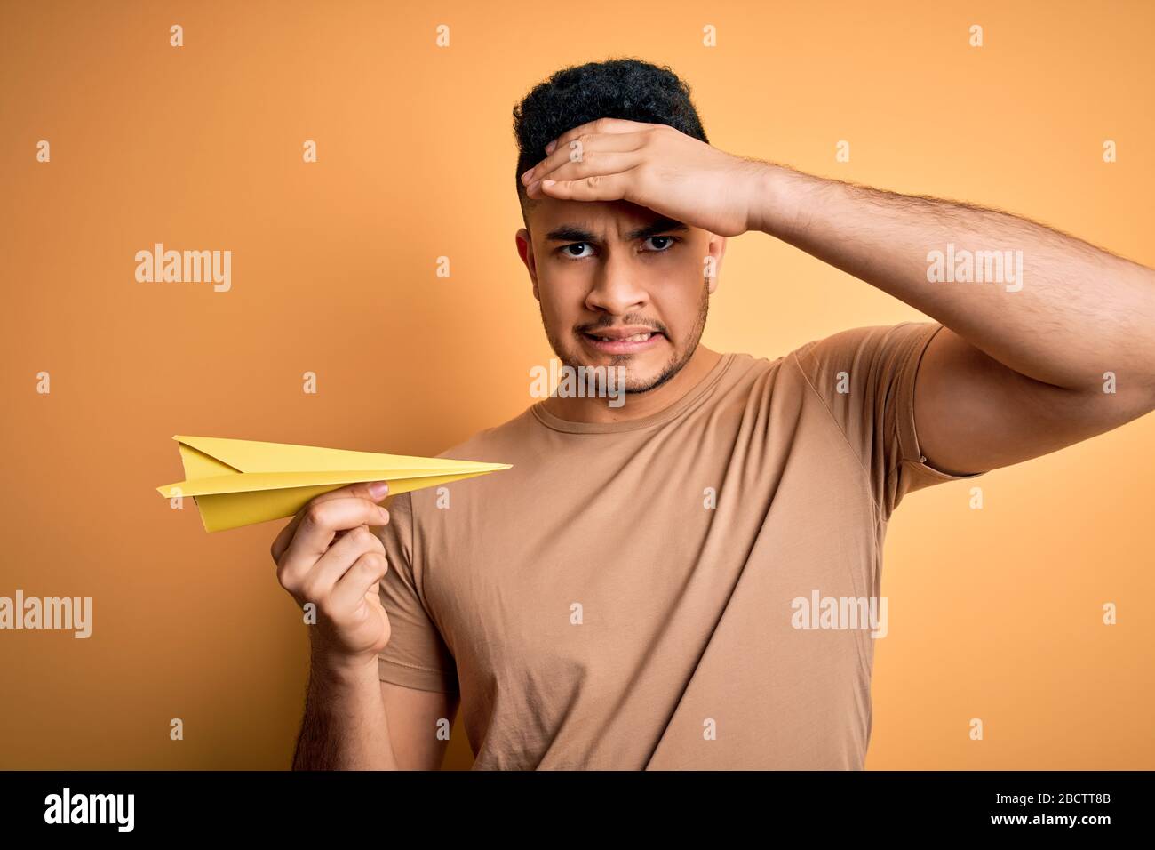 Young handsome man holding paper airplane over isolated yellow ...