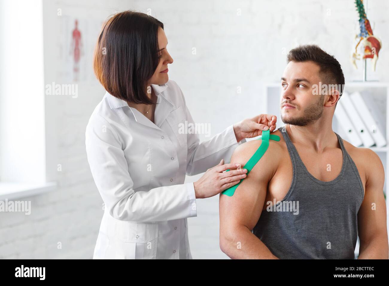 Kinesiology taping. Physical therapist applying kinesiology tape to patient shoulder. Female ...