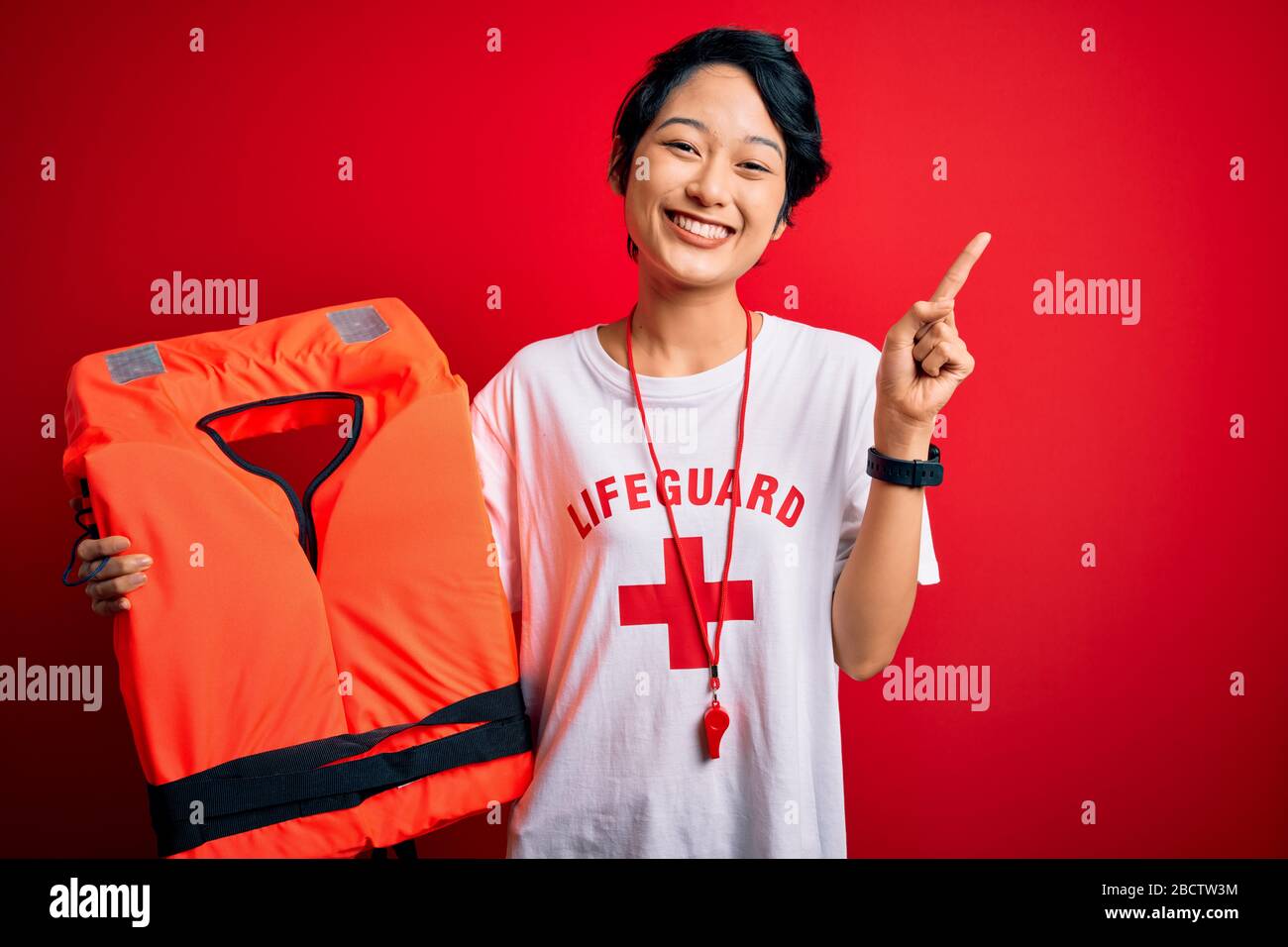 Young beautiful asian lifeguard girl using whistle holding orange life ...