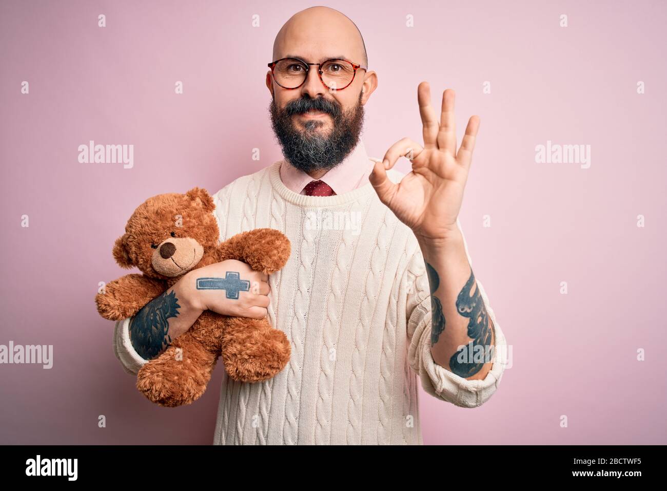 Handsome bald man with beard and tattoo holding teddy bear over ...