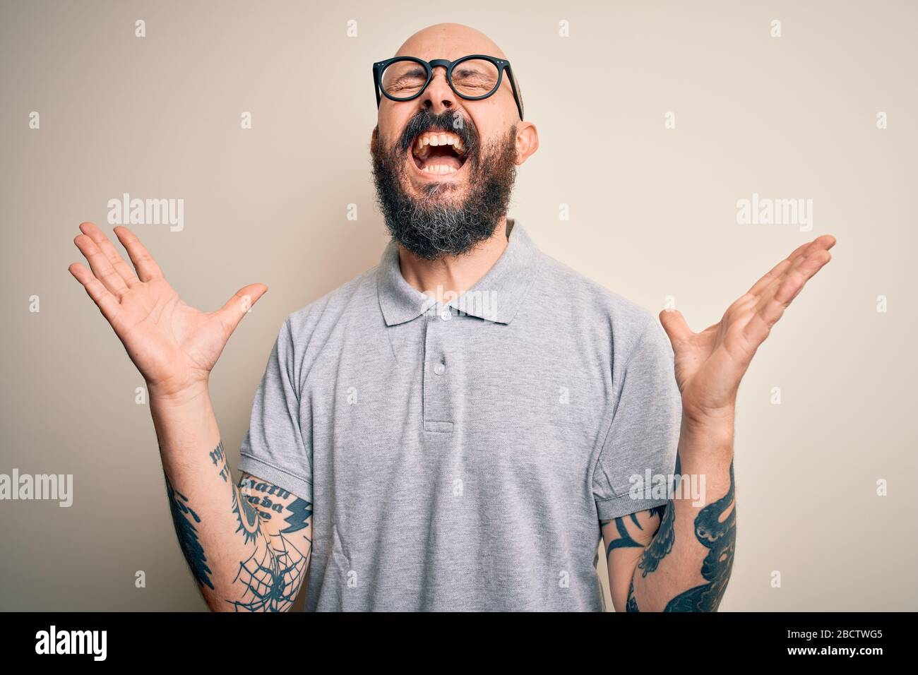 Handsome bald man with beard and tattoo wearing casual polo and glasses ...