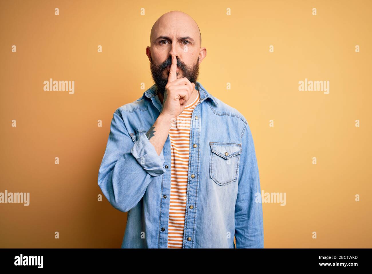 Handsome bald man with beard wearing casual denim jacket and striped t ...
