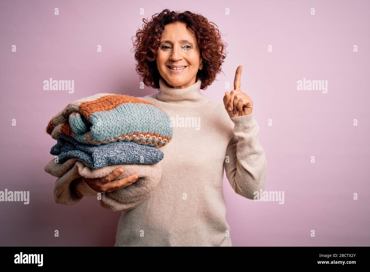 Middle age curly hair housework woman holding pile of clothes over ...