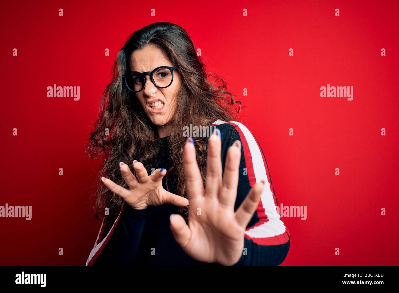 Young beautiful woman with curly hair wearing sweater and glasses over ...