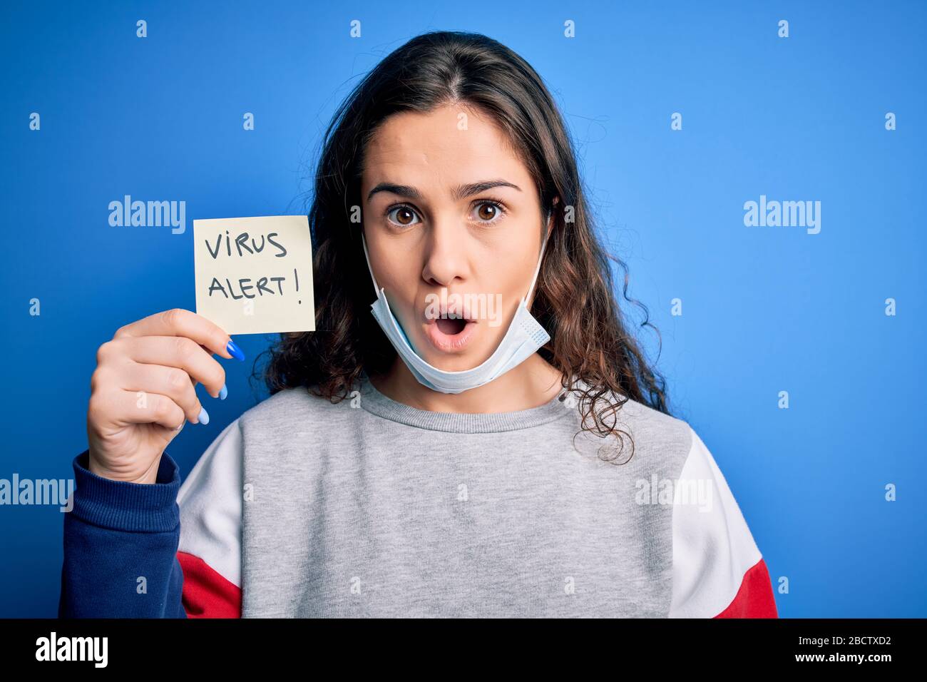 Young beautiful woman with curly hair wearing mask holding reminder ...