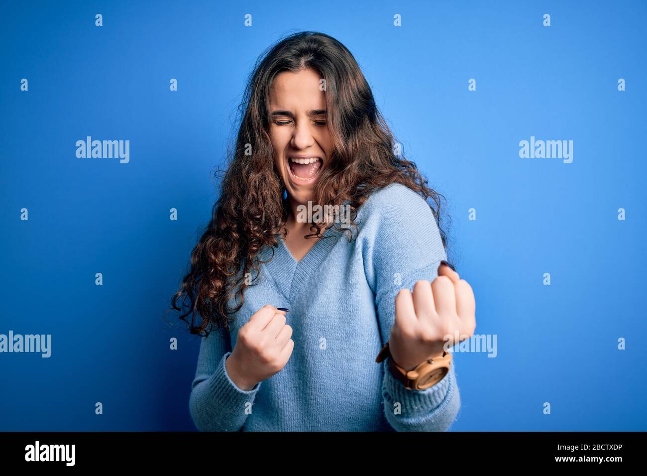 Young beautiful woman with curly hair wearing blue casual sweater over ...