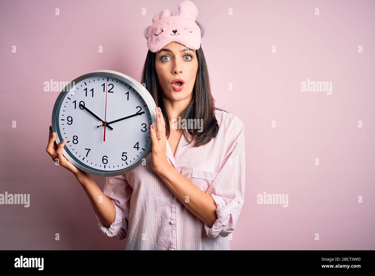 Young brunette woman with blue eyes wearing pajama holding big clock at ...
