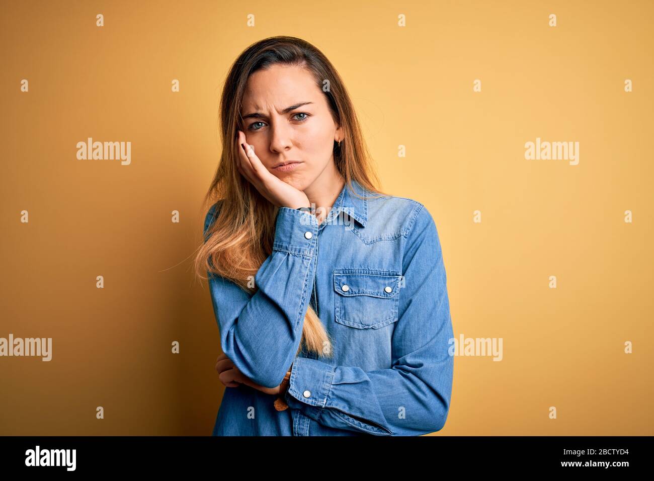 Young beautiful blonde woman with blue eyes wearing denim shirt over ...