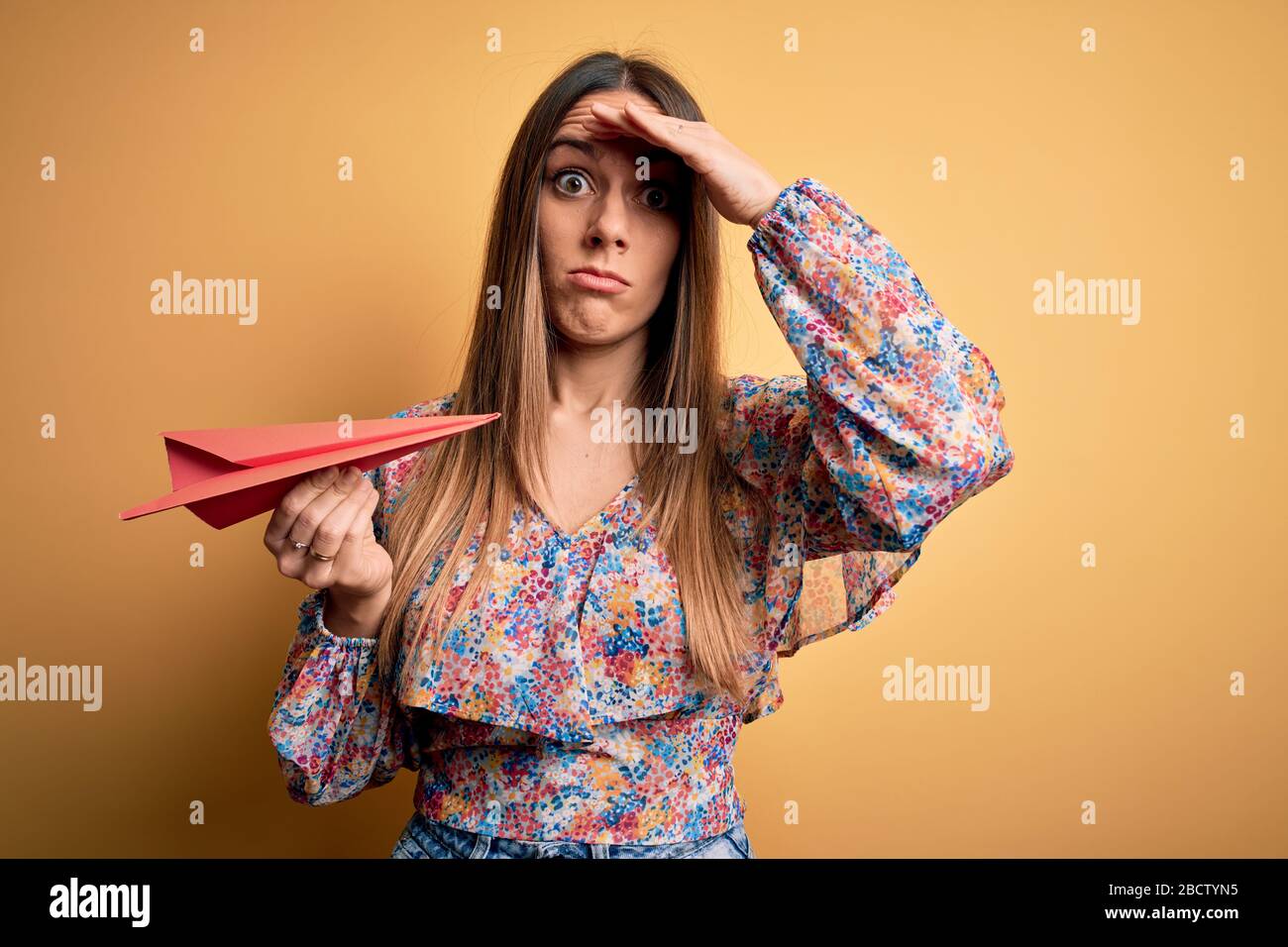 Young blonde woman holding paper plane over yellow isolated background ...