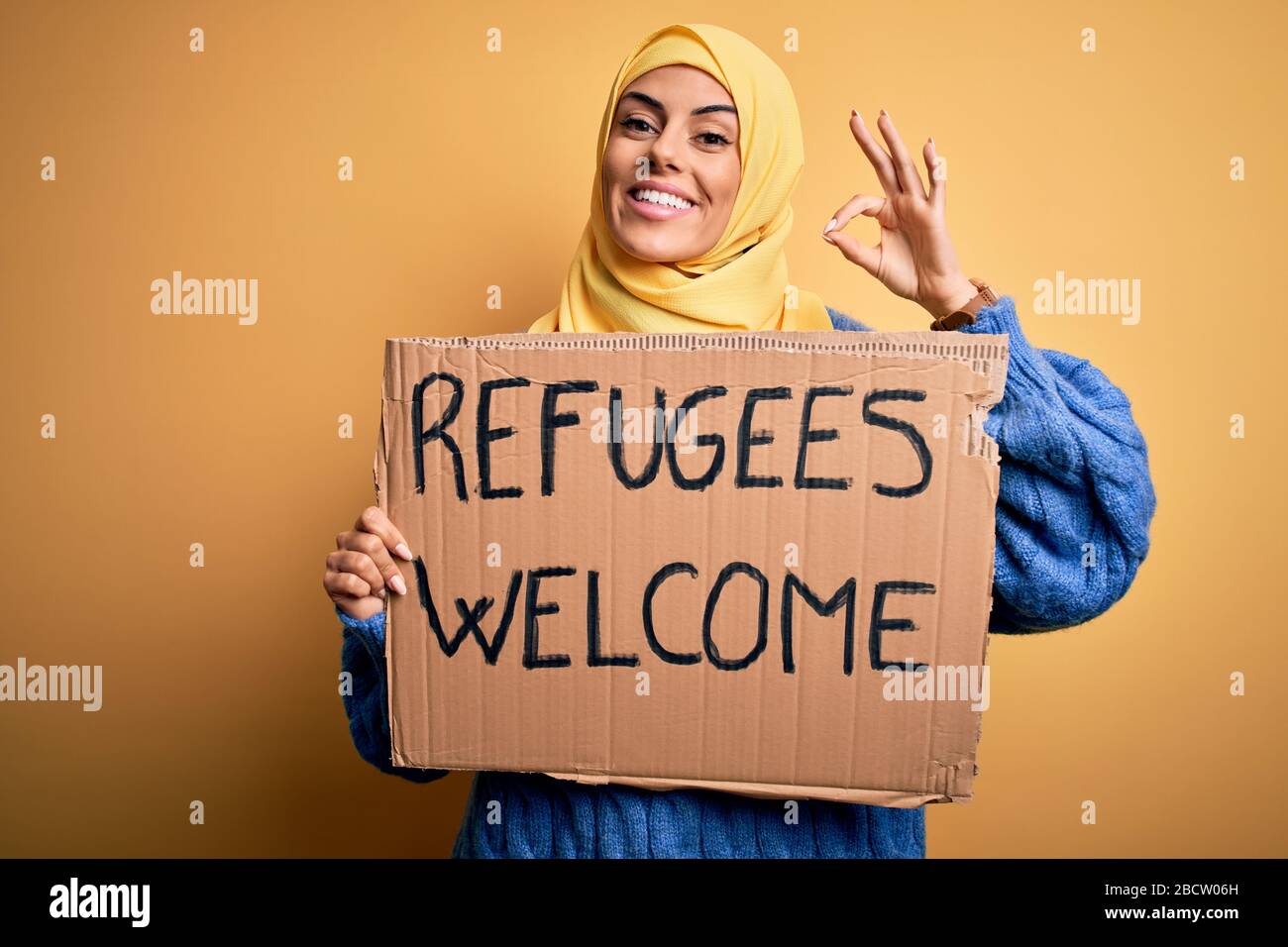 Beautiful arab woman wearing islamic hijab holding banner with refugees ...